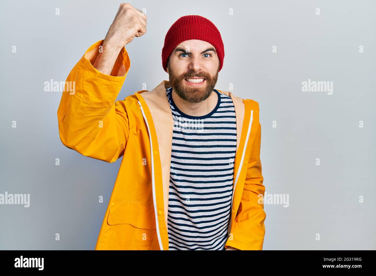 Caucasian man with beard wearing yellow raincoat angry and mad raising ...