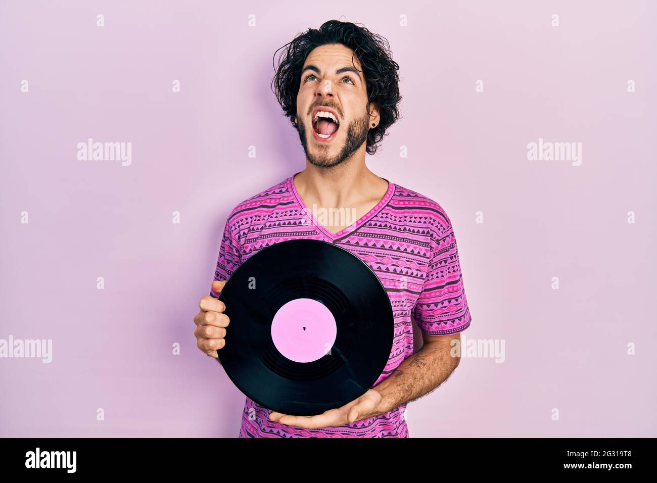 Handsome hispanic man holding vinyl disc angry and mad screaming ...