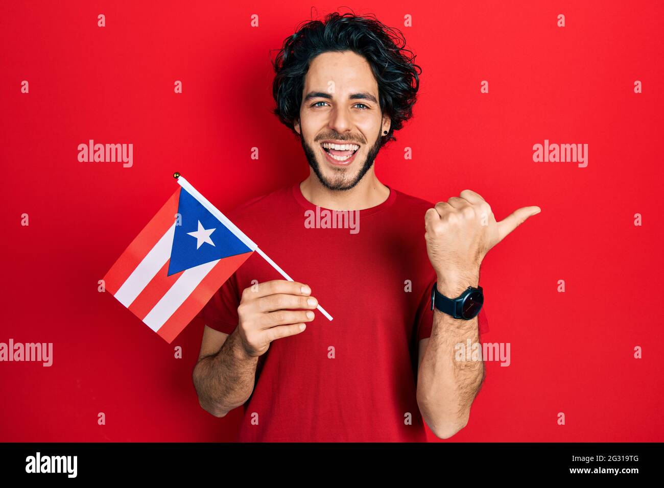 Handsome hispanic man holding puerto rico flag pointing thumb up to the ...
