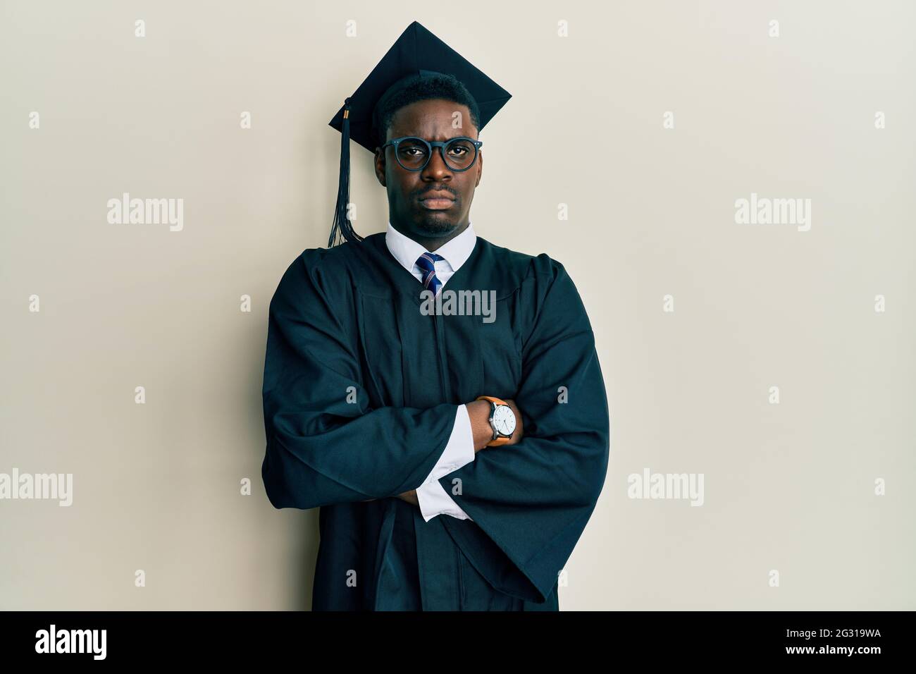 Handsome black man wearing graduation cap and ceremony robe skeptic and ...
