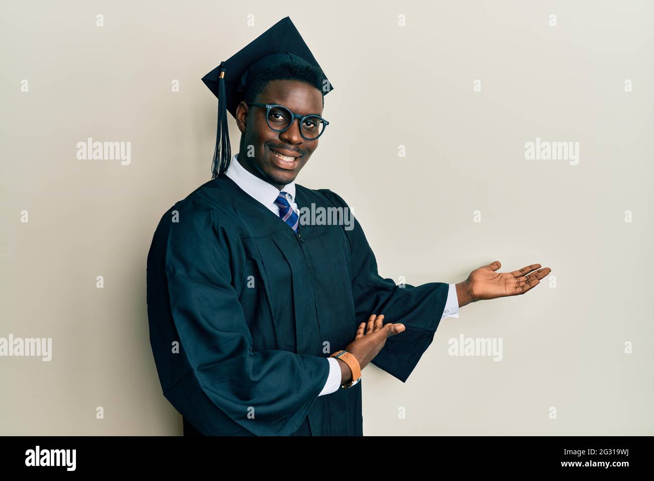 Handsome black man wearing graduation cap and ceremony robe inviting to ...