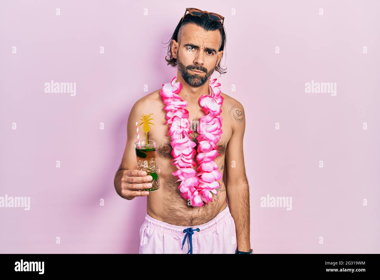 Young hispanic man wearing swimsuit and hawaiian lei drinking tropical ...