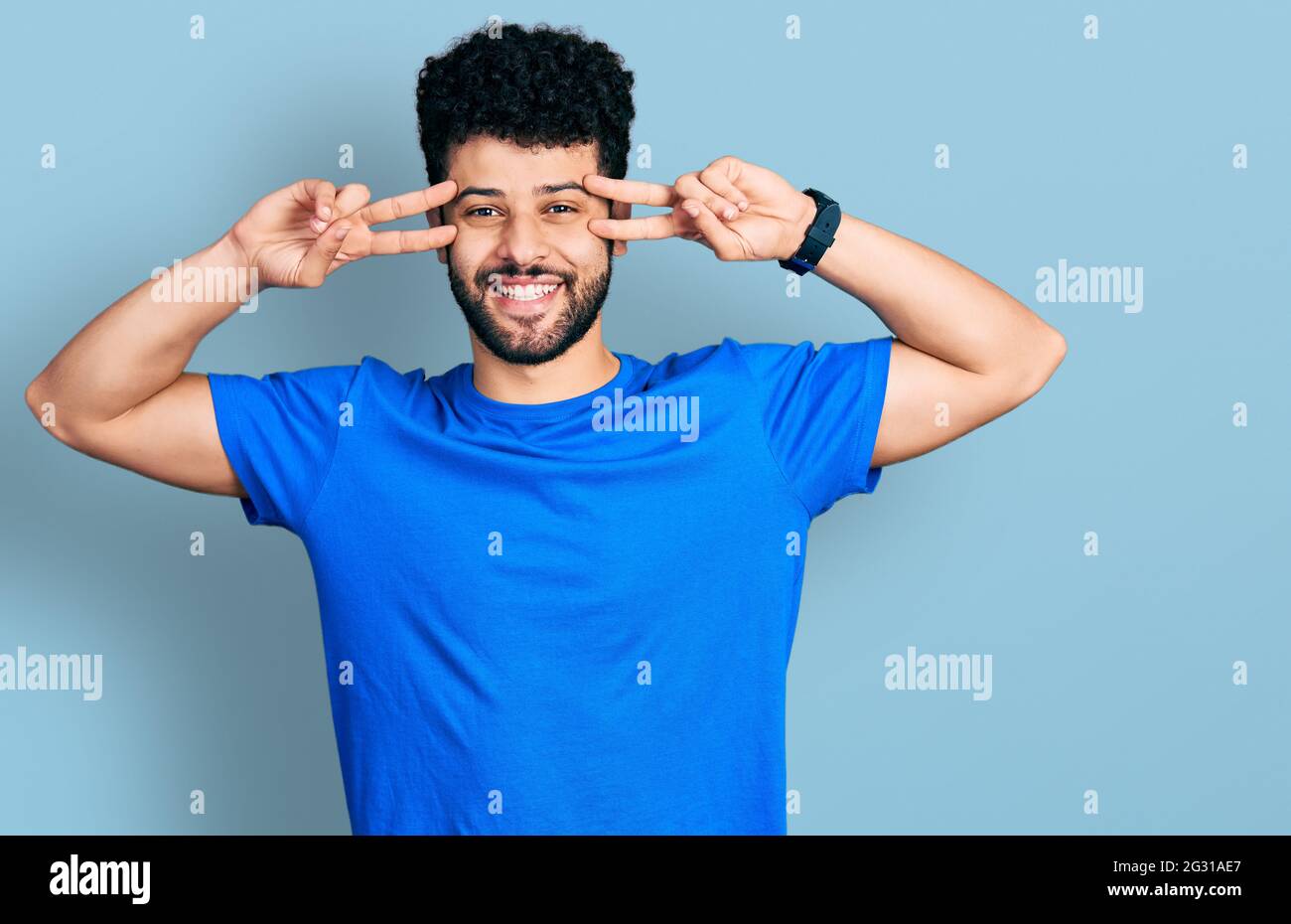 Young arab man with beard wearing casual blue t shirt doing peace ...