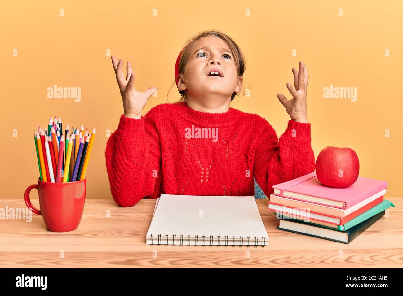 Little beautiful girl sitting on classroom desk crazy and mad shouting ...