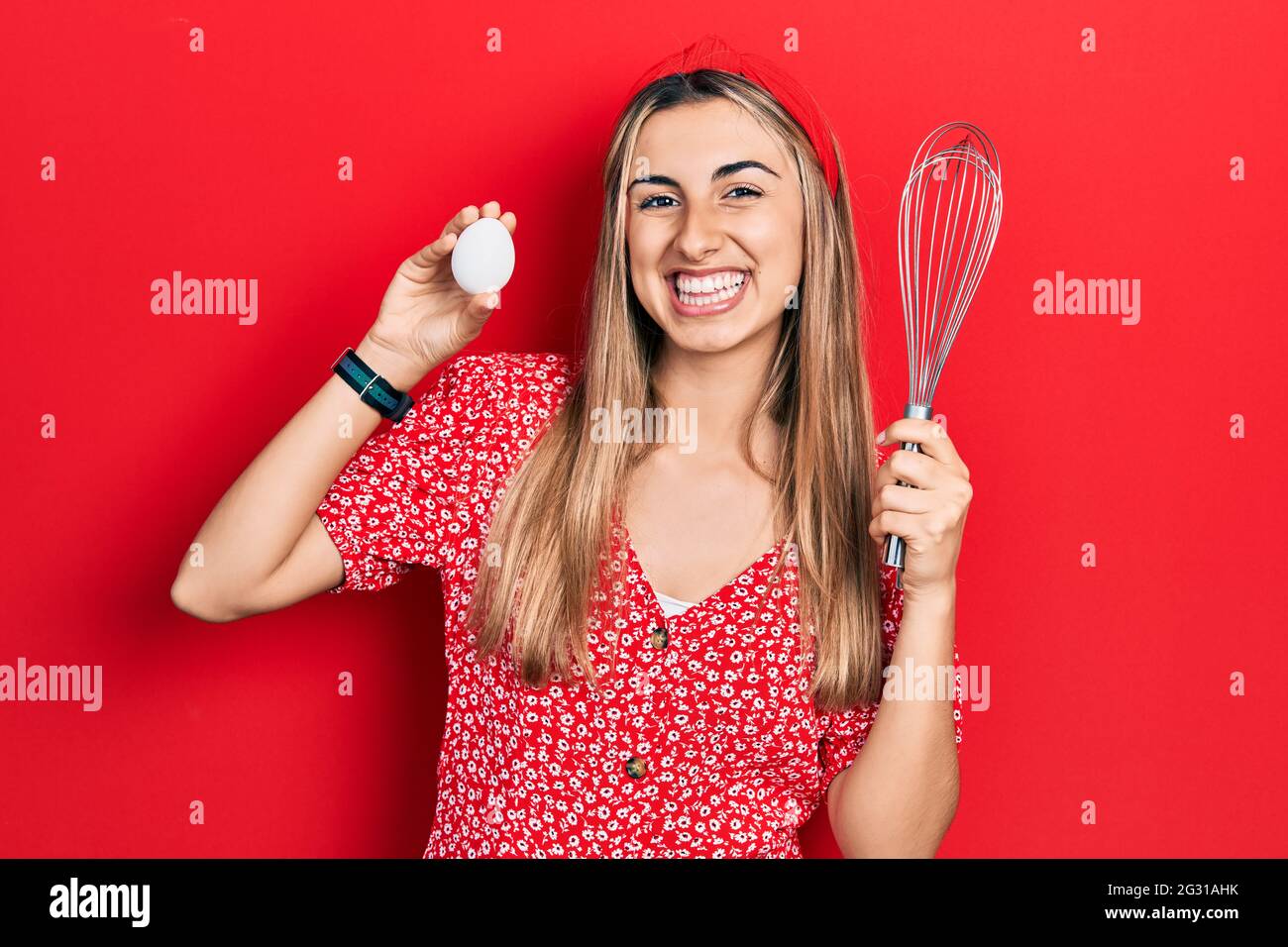 Beautiful hispanic woman holding egg and baker whisk smiling with a ...