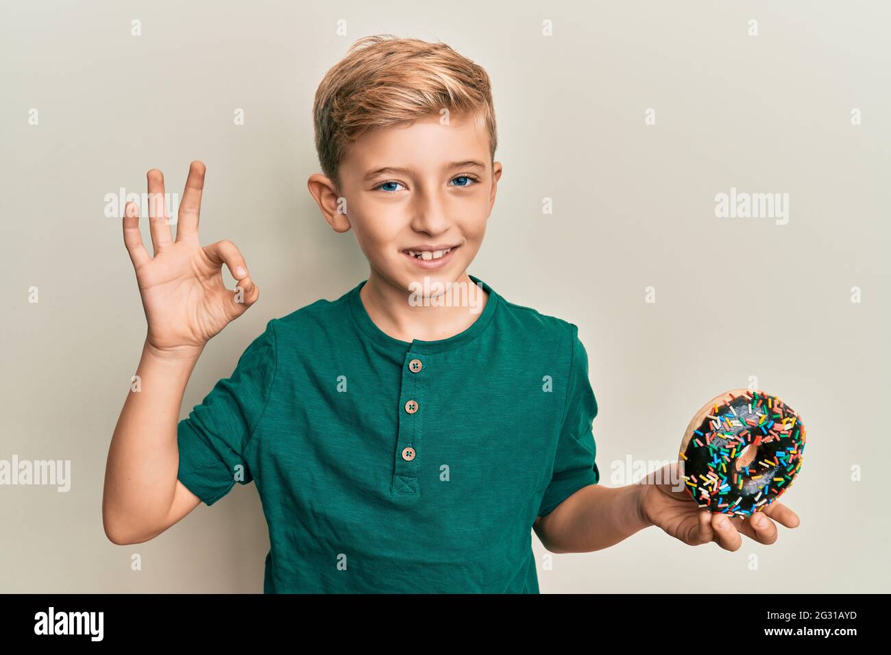 Little caucasian boy kid holding chocolate doughnut doing ok sign with ...
