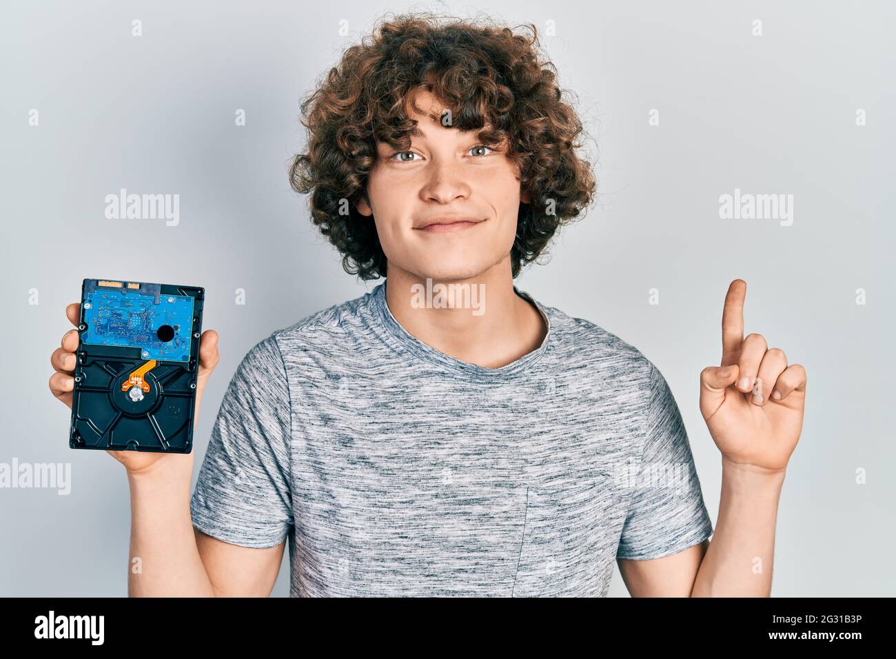 Handsome young man holding hdd disk smiling with an idea or question ...