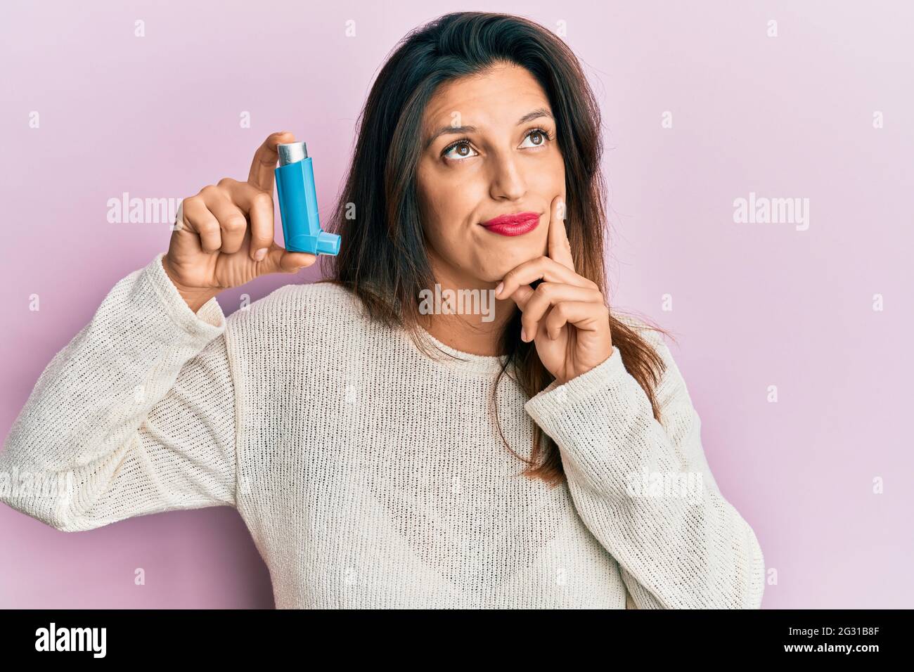 Beautiful hispanic woman holding medical asthma inhaler serious face ...