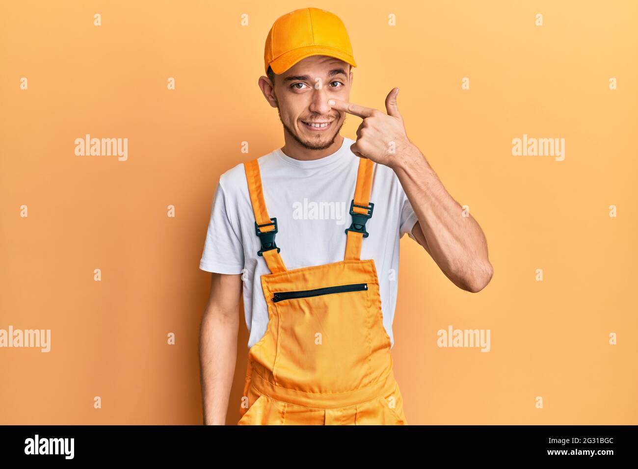 Hispanic young man wearing handyman uniform pointing with hand finger ...