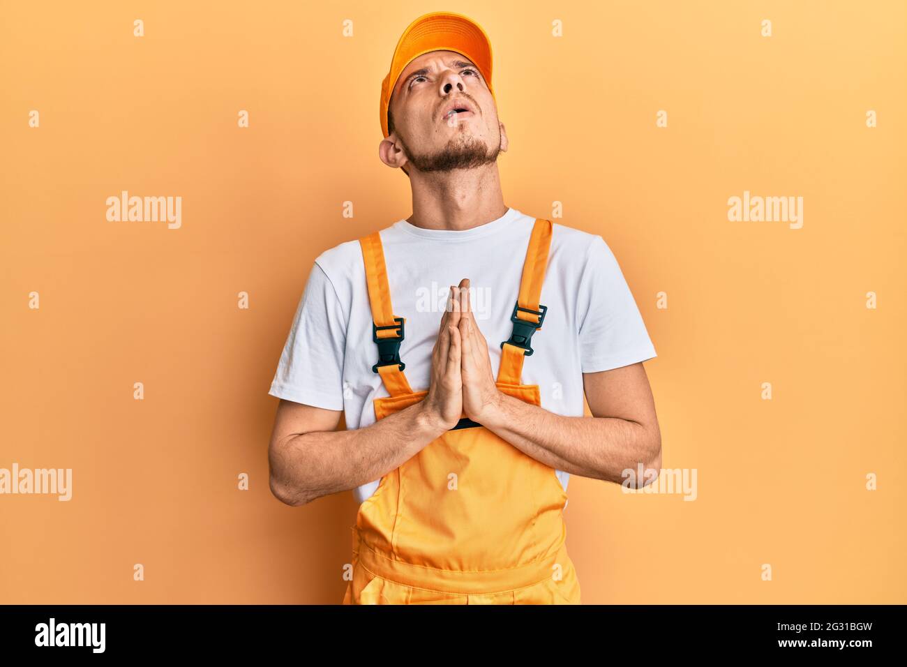 Hispanic young man wearing handyman uniform begging and praying with ...
