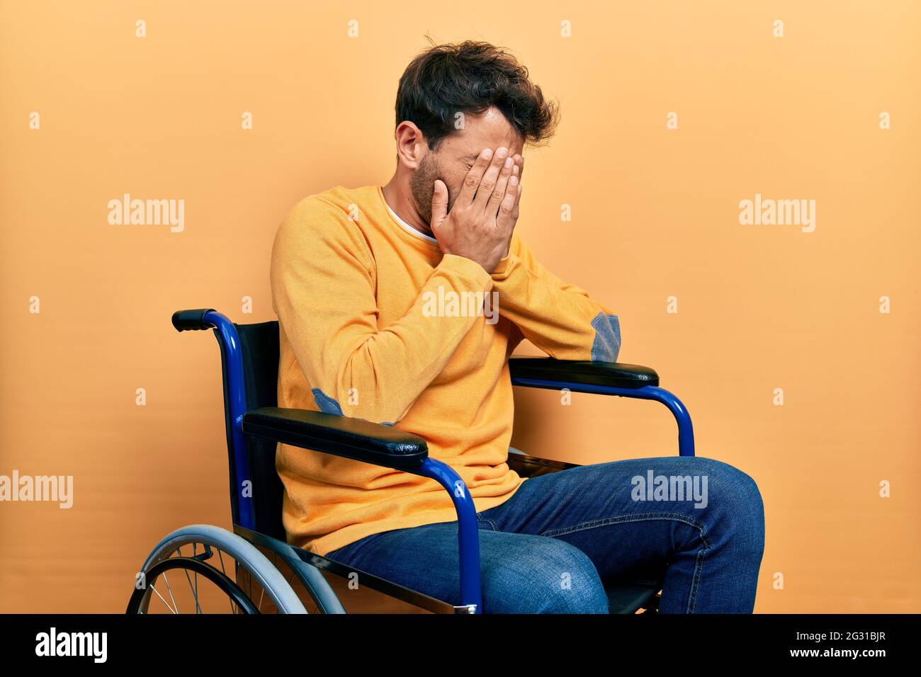 Handsome man with beard sitting on wheelchair with sad expression ...