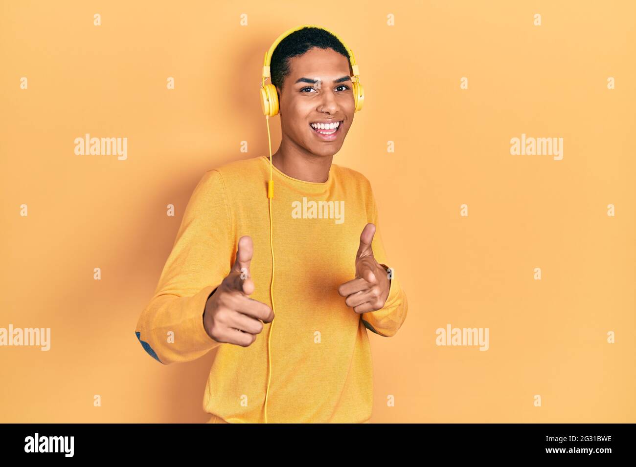 Young african american guy listening to music using headphones pointing ...