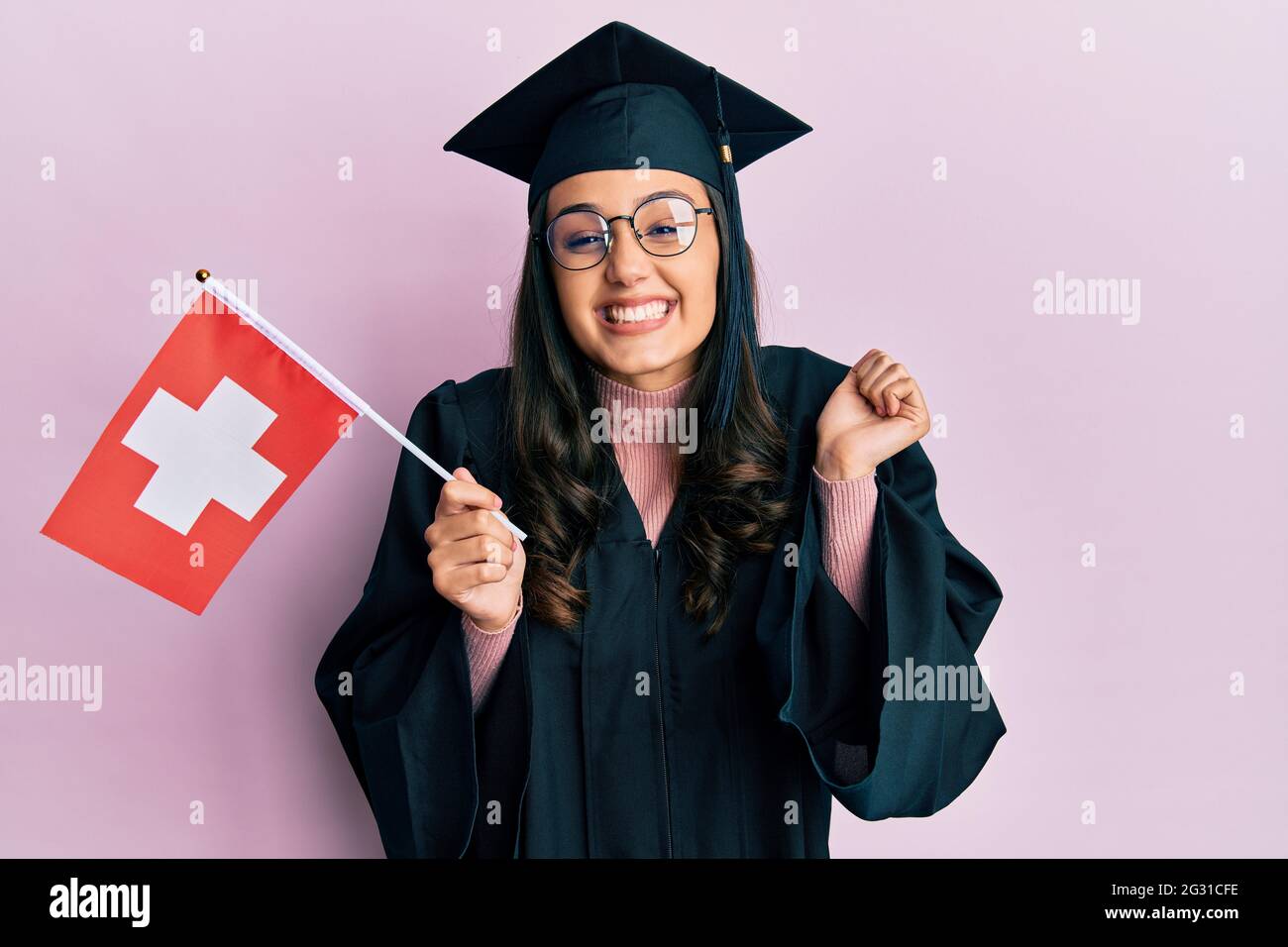 Young hispanic woman wearing graduation uniform holding switzerland ...