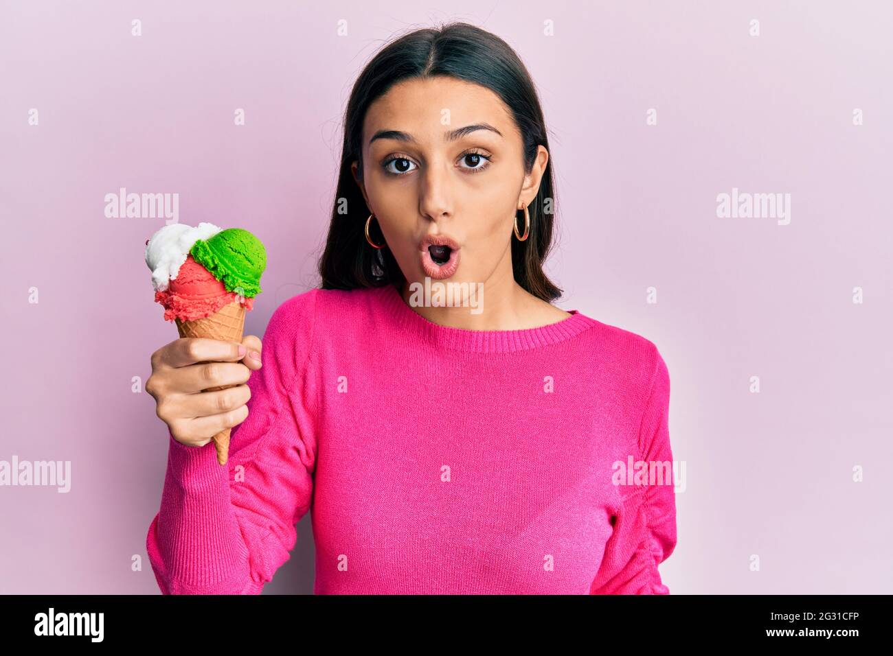 Young hispanic woman holding ice cream scared and amazed with open ...