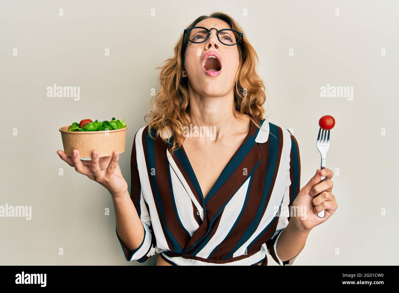 Young caucasian woman wearing business clothes eating salad angry and ...