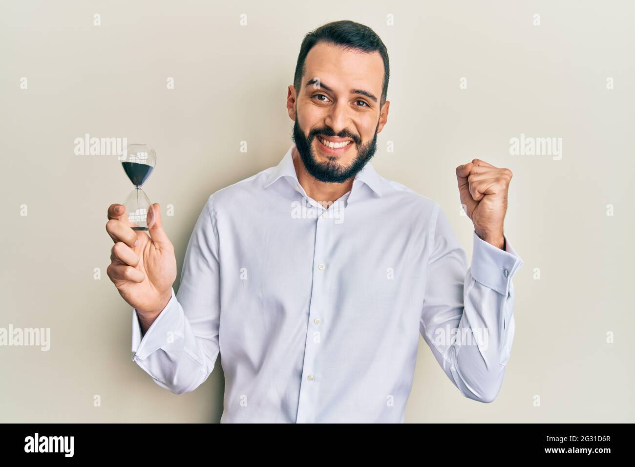 Young man with beard holding sand clock screaming proud, celebrating ...