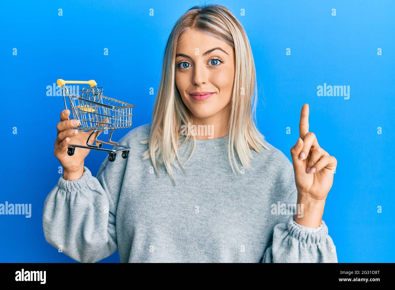 Beautiful blonde woman holding small supermarket shopping cart smiling ...