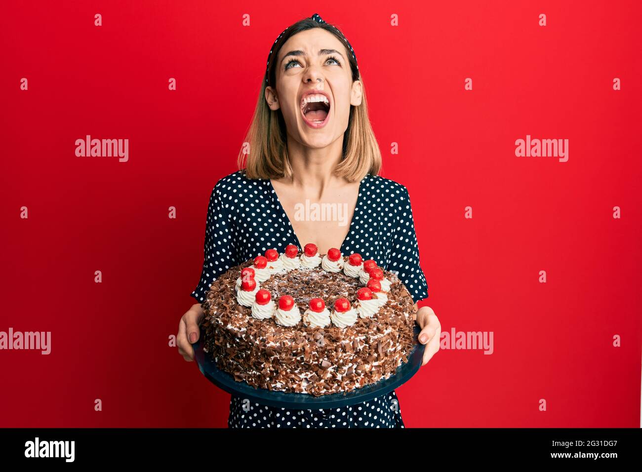 Young caucasian blonde woman holding chocolate cake angry and mad ...