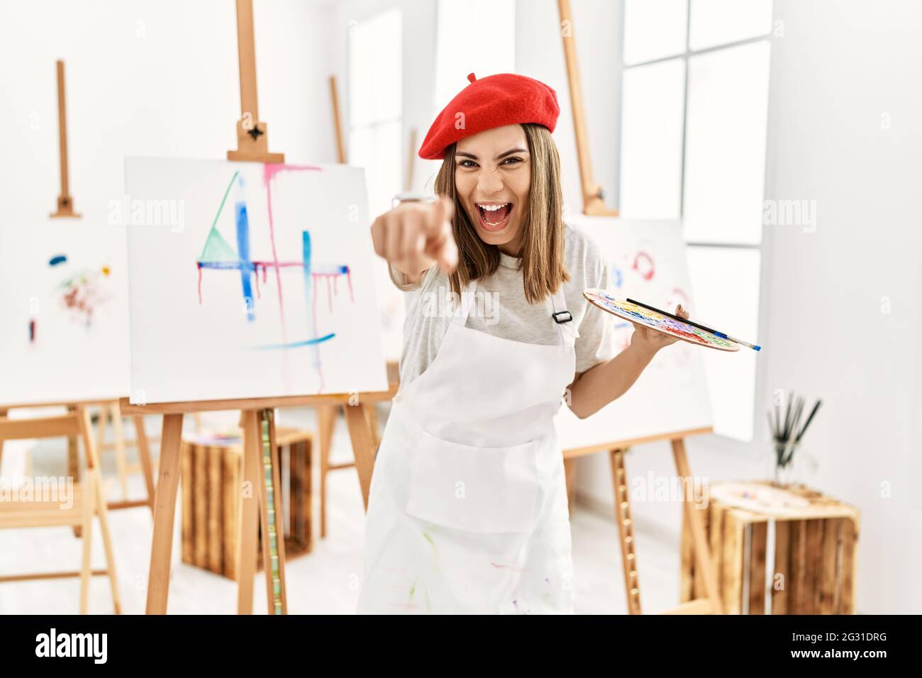 Young artist woman painting on a canvas at art studio pointing ...
