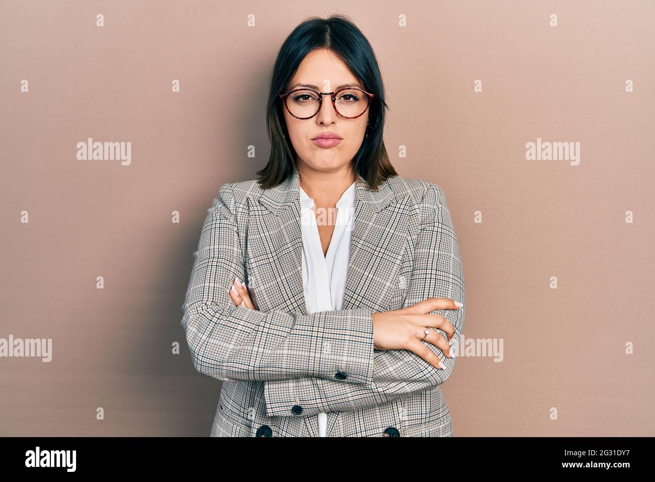 Young hispanic woman wearing business clothes and glasses skeptic and nervous, disapproving ...