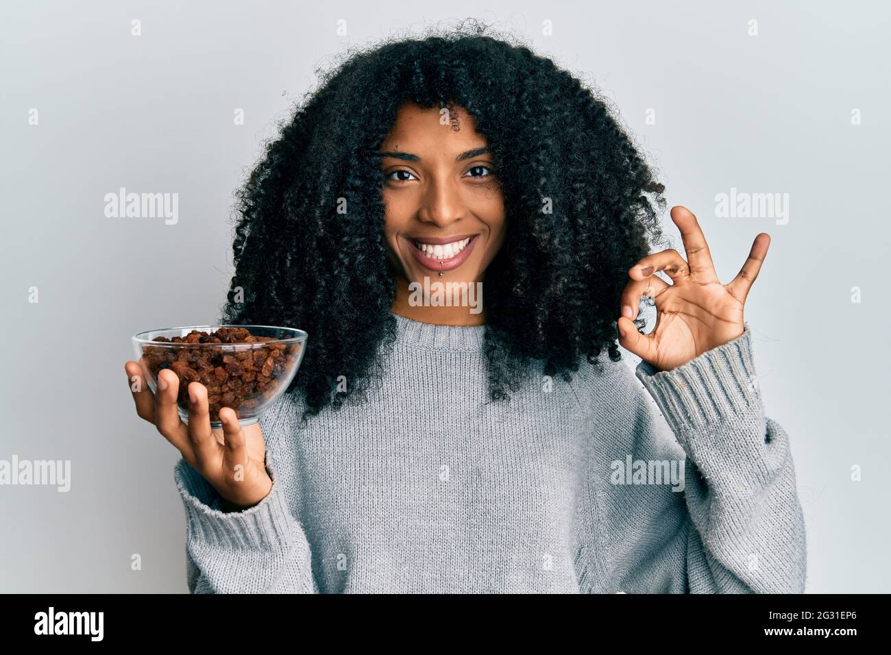 African american woman with afro hair holding raisins in bowl doing ok ...