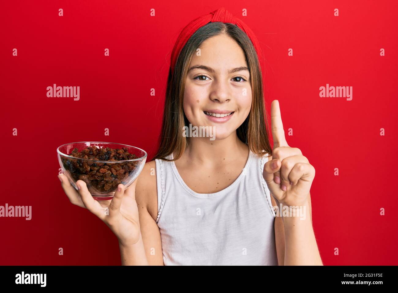 Beautiful brunette little girl holding bowl of raisins smiling with an ...
