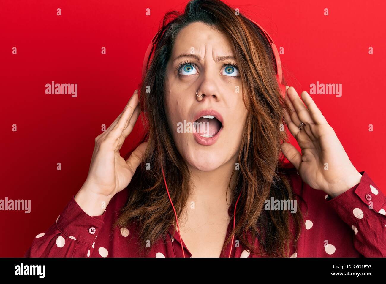 Young caucasian woman listening to music using headphones angry and mad ...