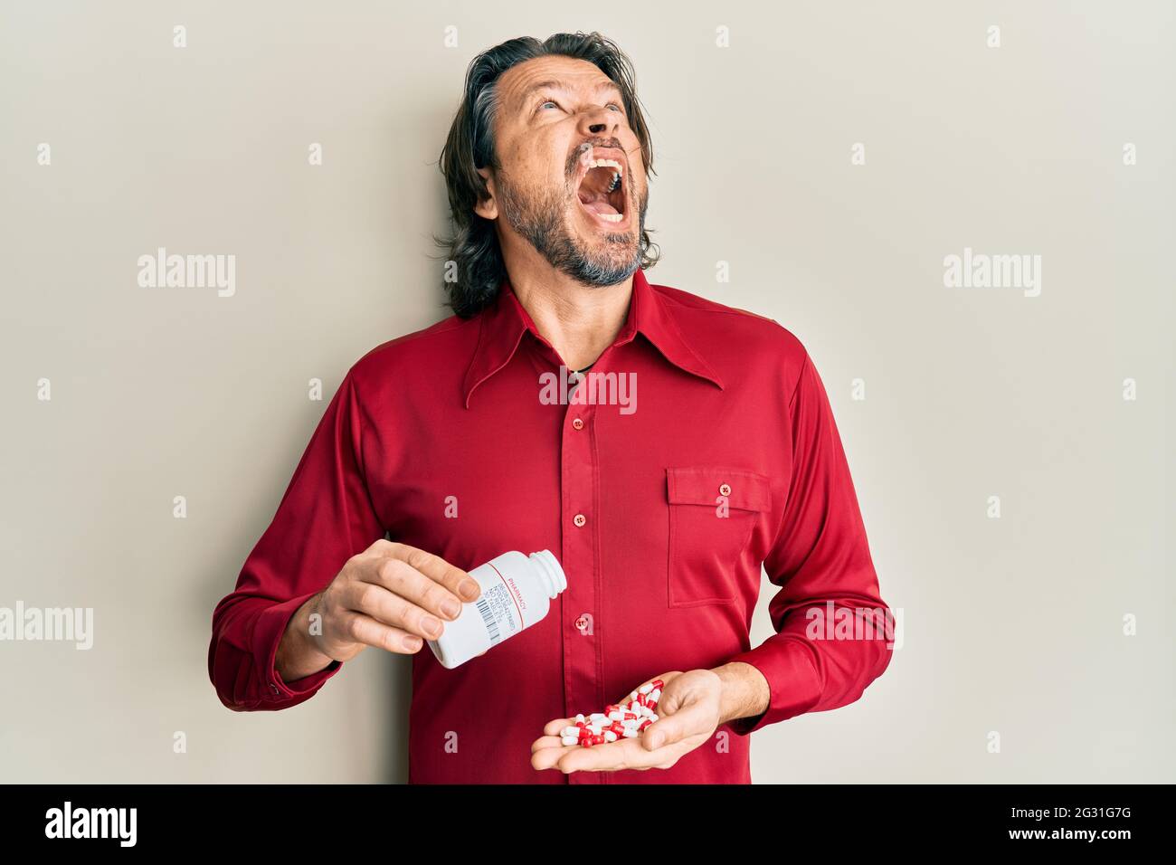 Middle age handsome man taking pills angry and mad screaming frustrated ...