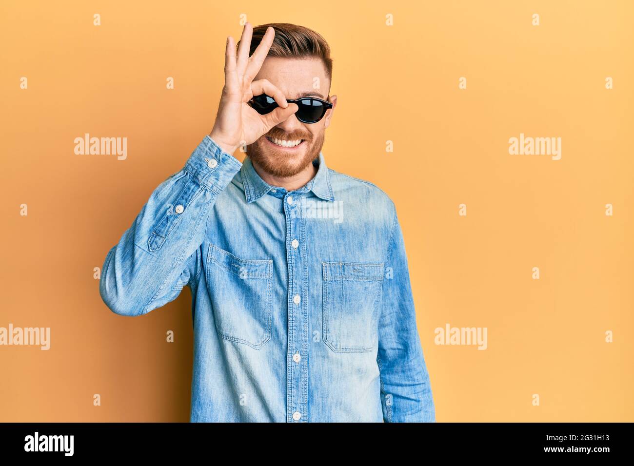 Young redhead man wearing stylish sunglasses smiling happy doing ok ...