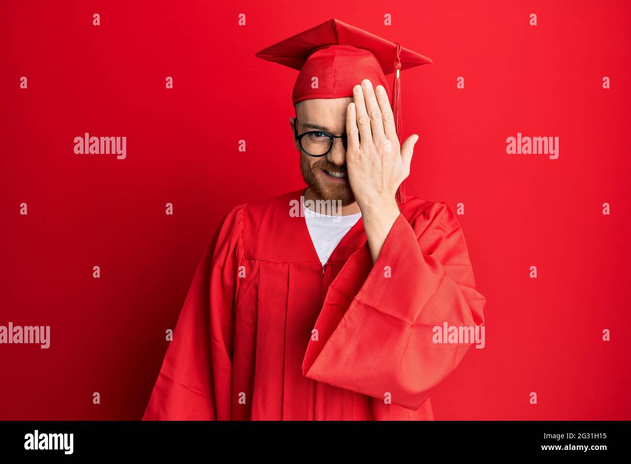 Young redhead man wearing red graduation cap and ceremony robe covering ...