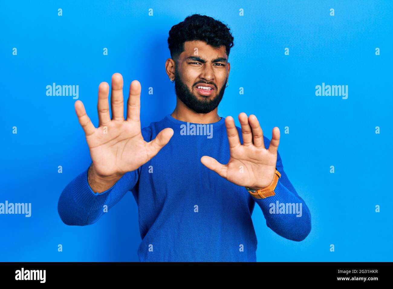 Arab man with beard wearing casual blue sweater afraid and terrified ...