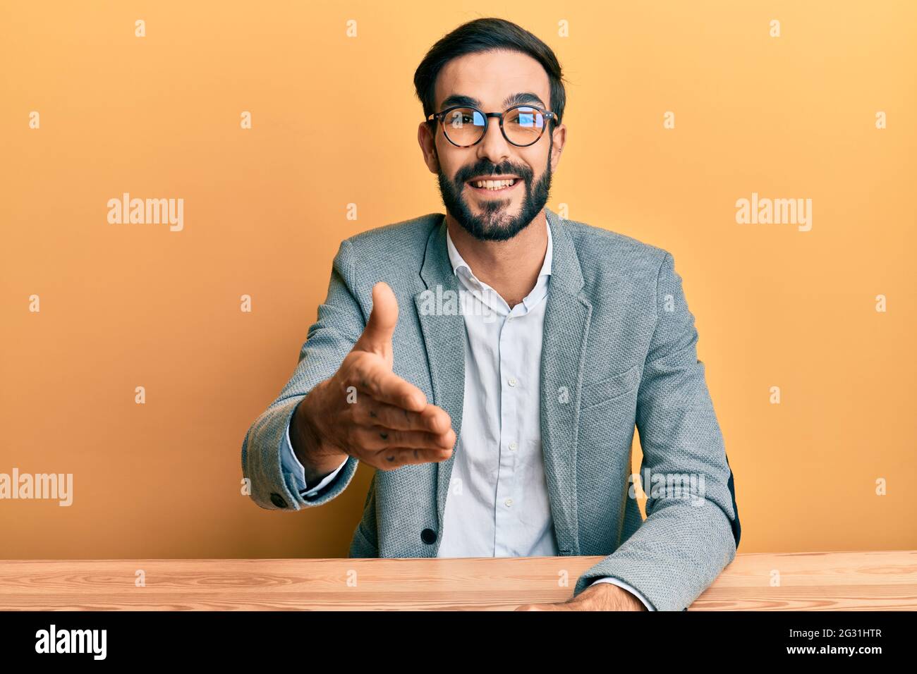 Young hispanic man working at the office smiling friendly offering ...