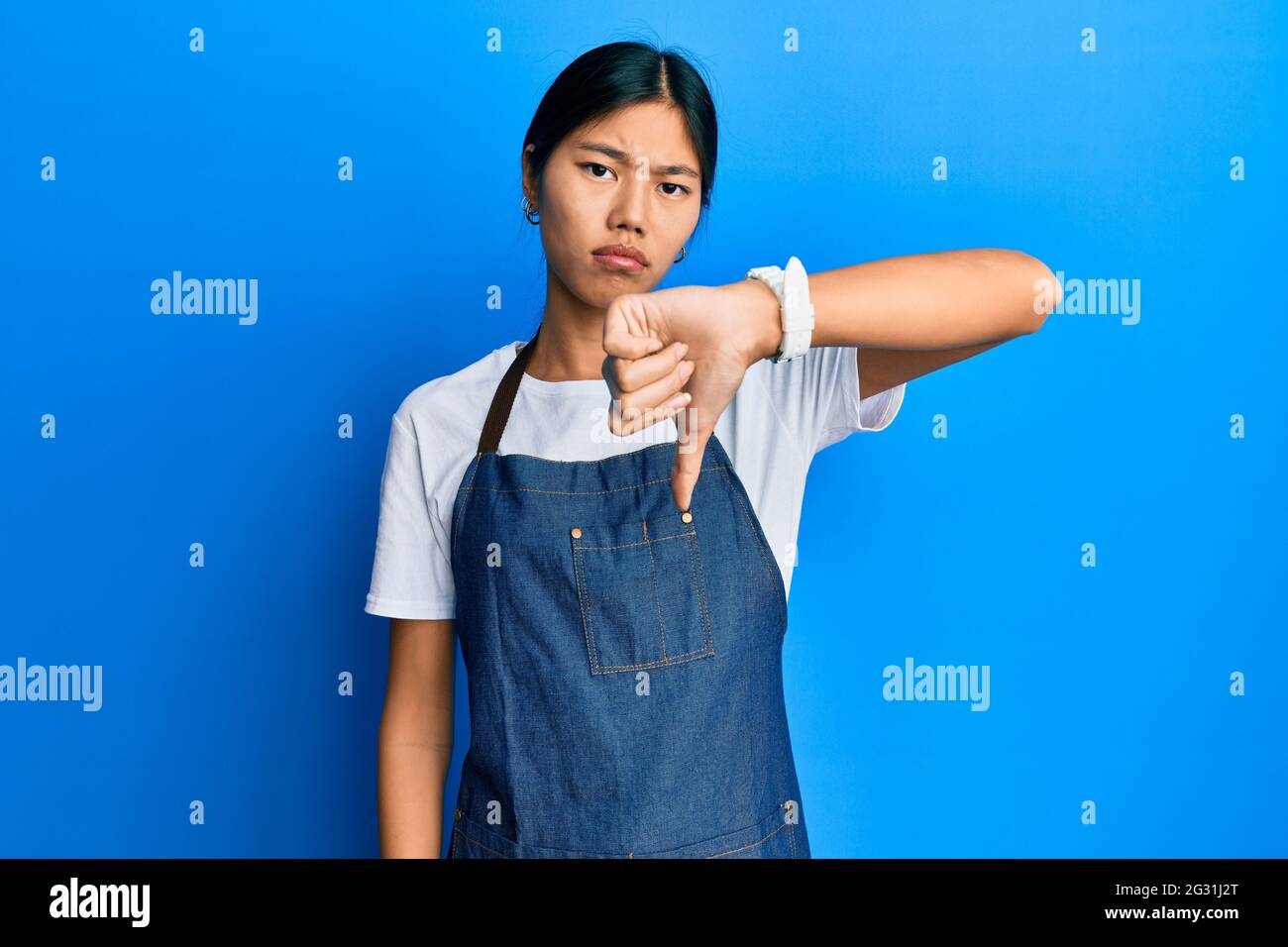 Young chinese woman wearing waiter apron looking unhappy and angry ...