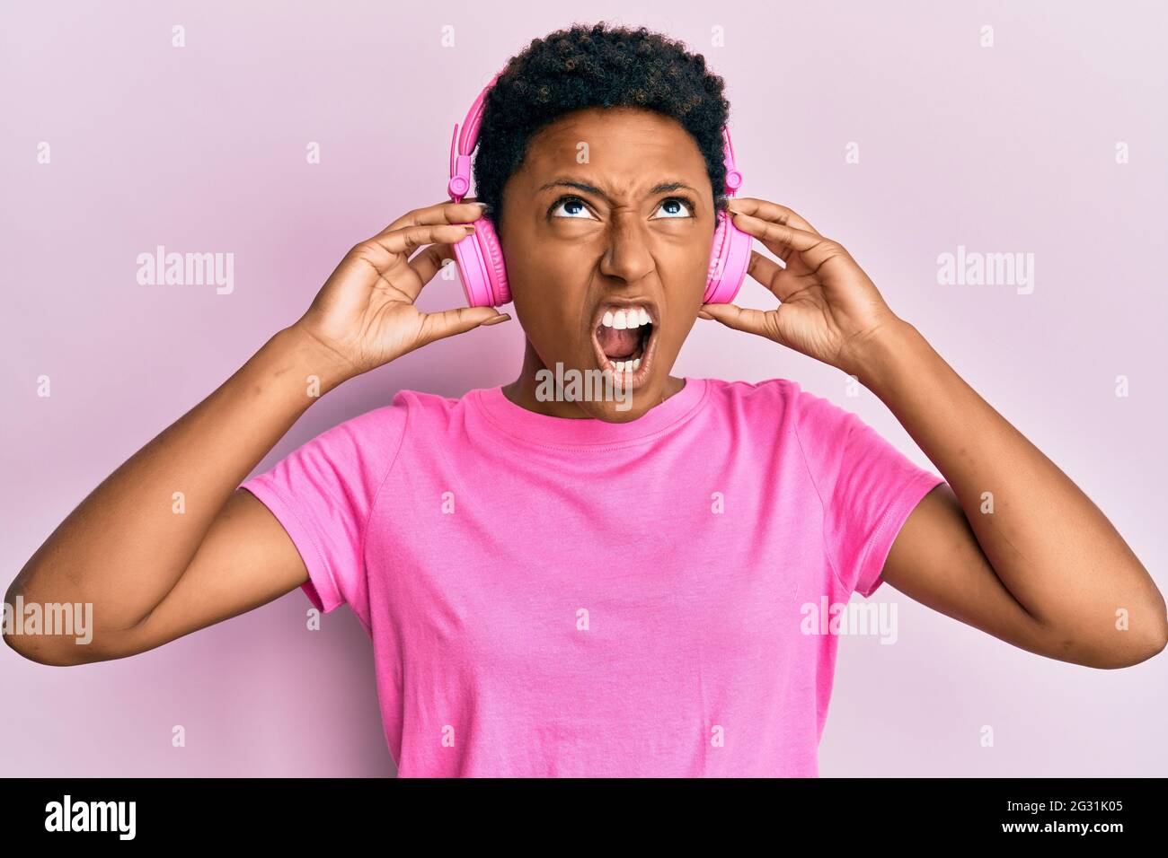 Young african american girl listening to music using headphones angry ...