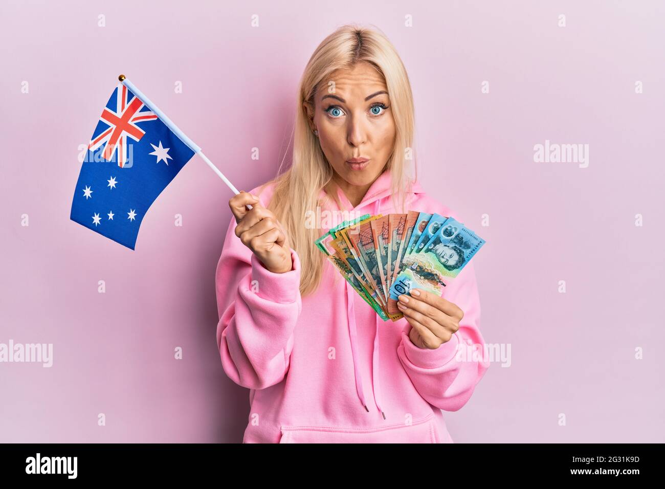Young blonde woman holding australian flag and dollars in shock face ...