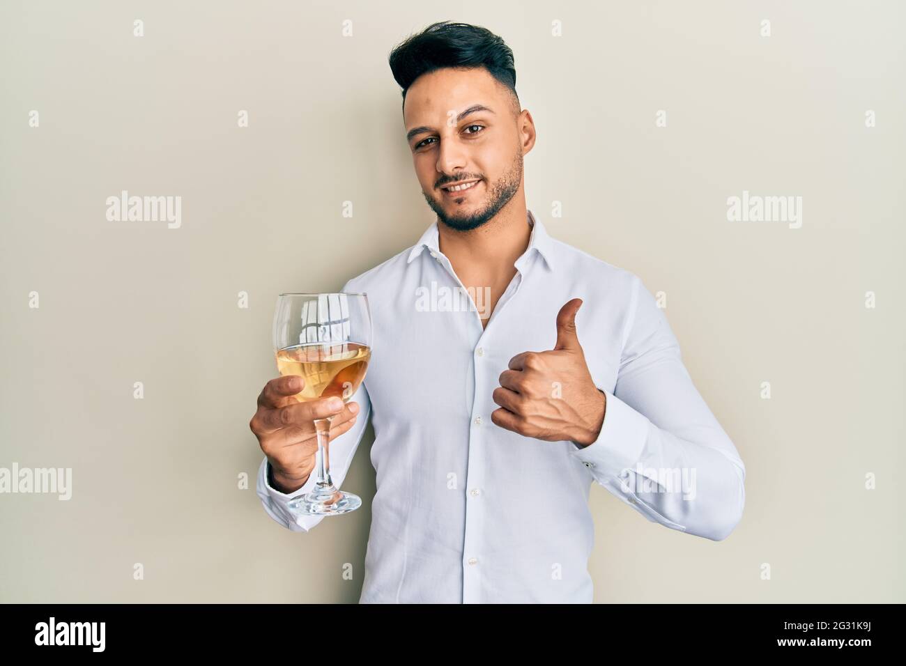 Young arab man drinking a glass of white wine smiling happy and ...