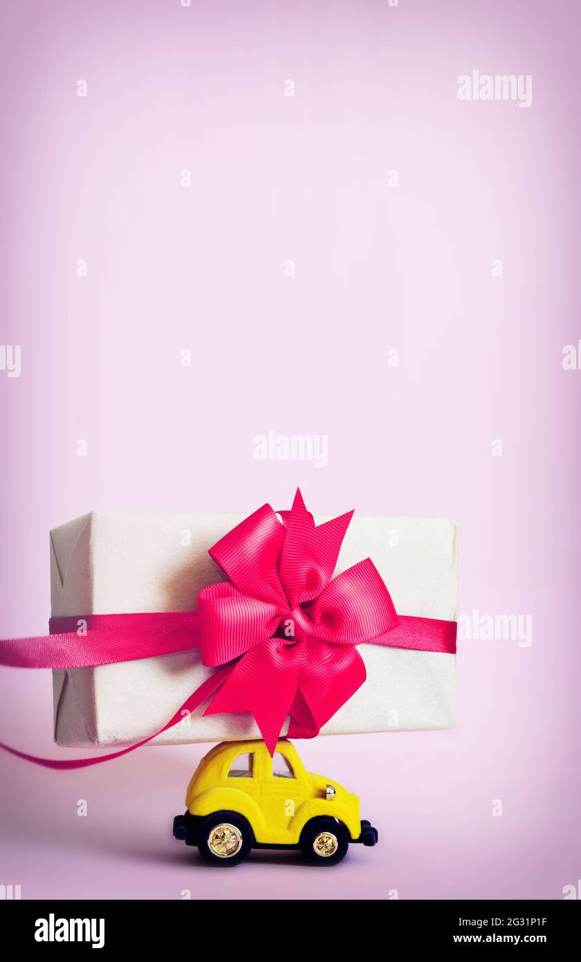 Yellow toy retro car with gift box on a roof on pink background. Copy ...
