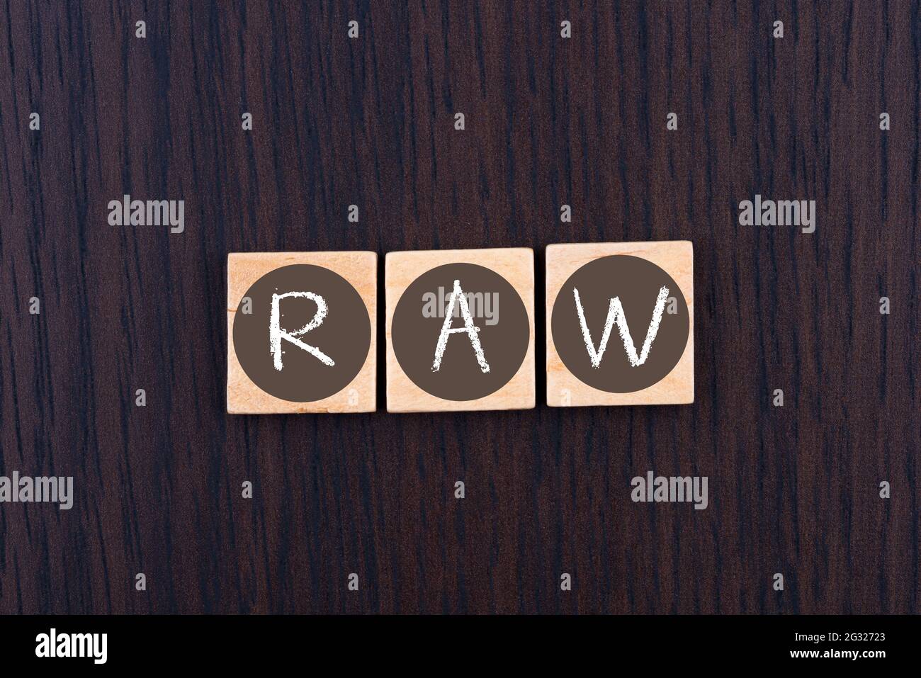 A top view of 3 wooden blocks with the word raw isolated on a dark ...