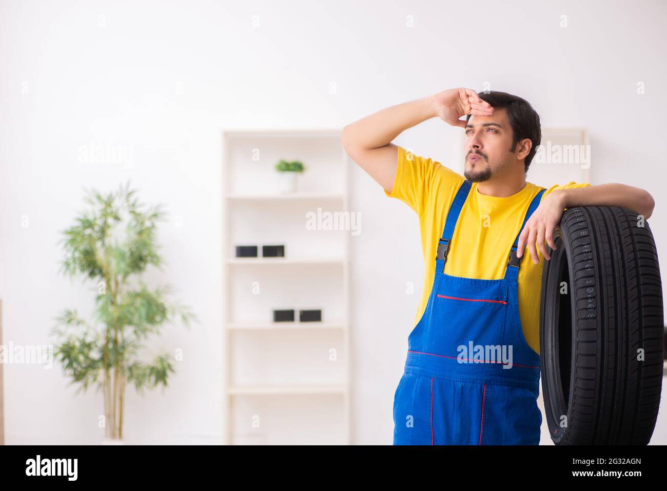 Young garage worker with tyre at workshop Stock Photo - Alamy