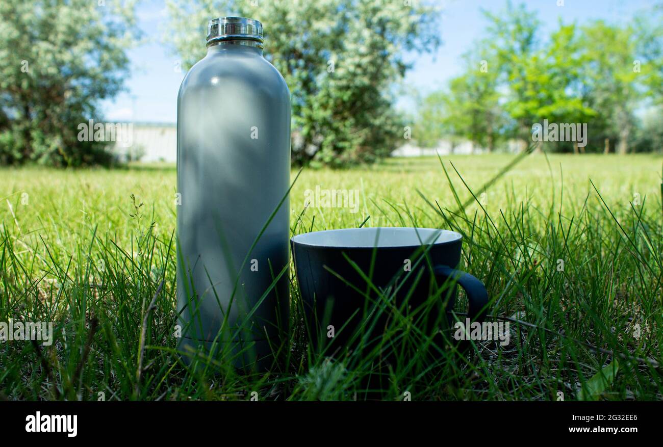 Thermos and a mug in the grass. Camping. A mug with tea in a green ...