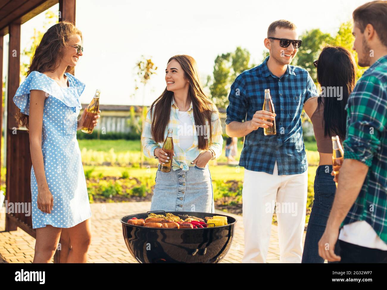Group of people standing around a barbecue, grilling outdoors, chatting ...
