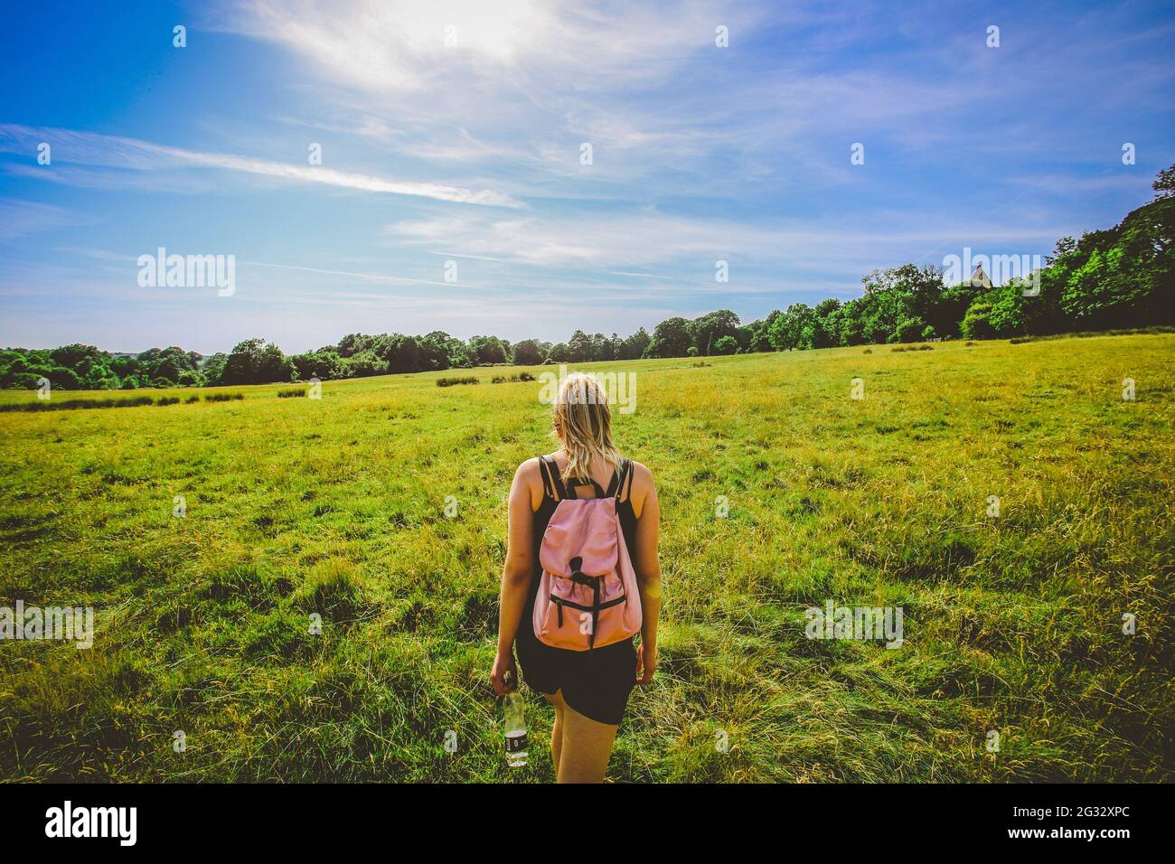 A female with a backpack walking on the green meadow in the scenic countryside Stock Photo - Alamy