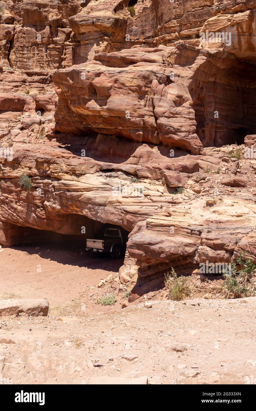 Pickup truck parked in the shadow of cave carved in big sandstone rock ...