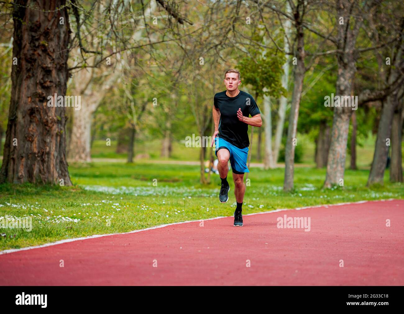 Positive young man keeping active lifestyle and jogging along city park ...