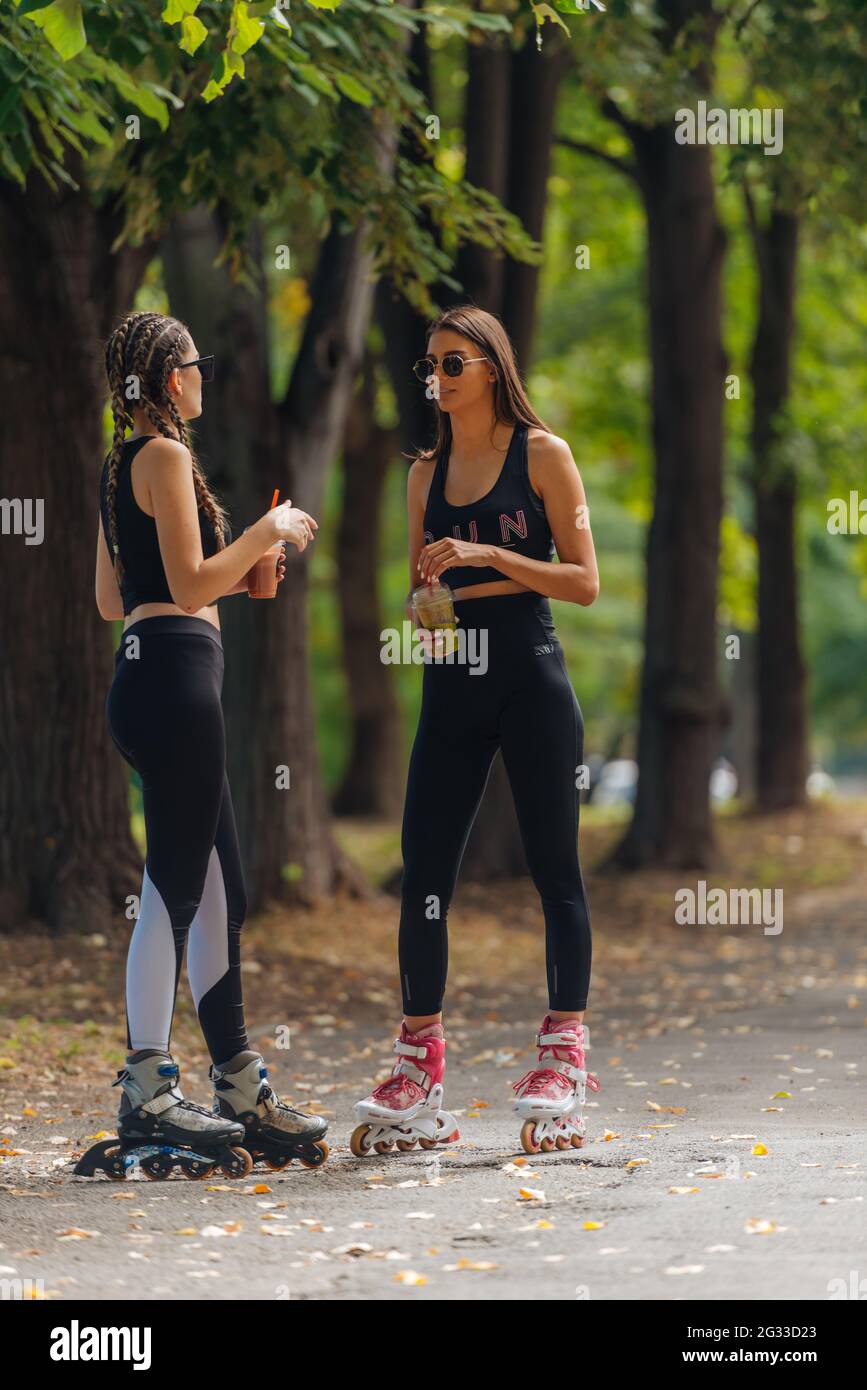 Two women in sportswear rollerblading at the park in sunny weather ...