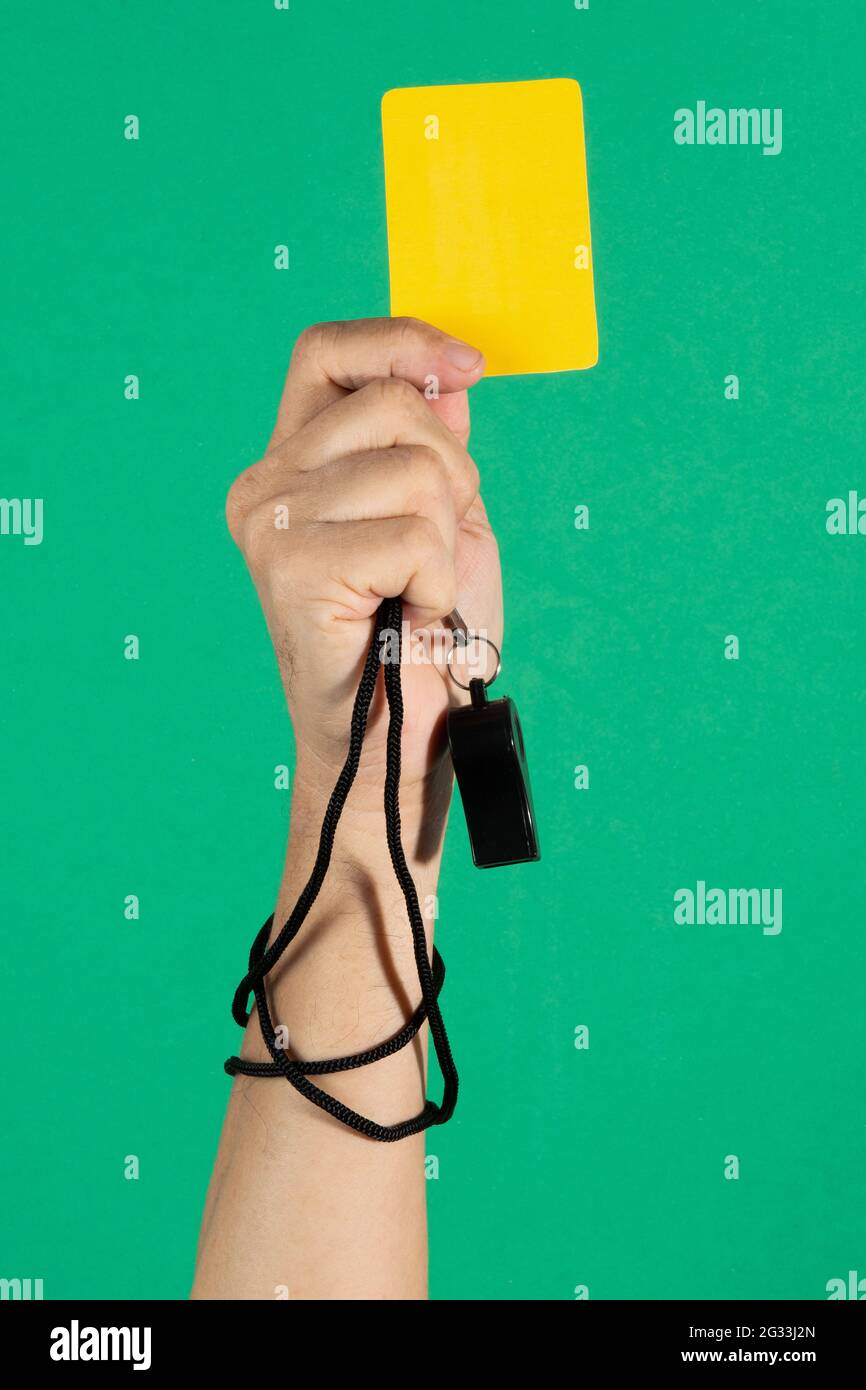 referee's hand holding a yellow card and whistle on green background ...