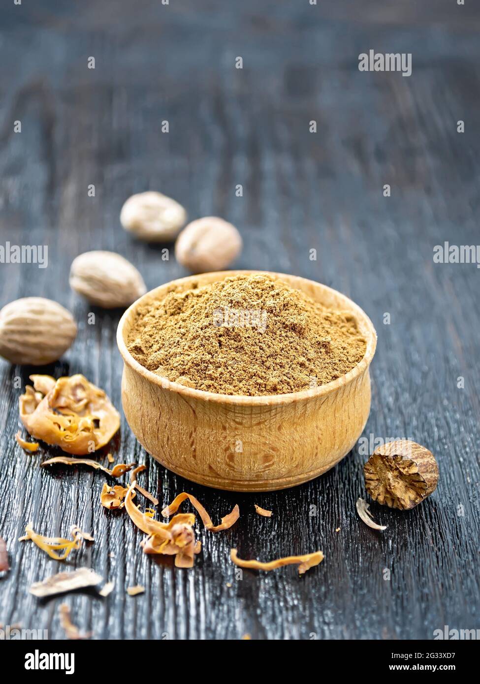 Ground nutmeg in a bowl, dried nutmeg arillus, whole nuts on a dark ...