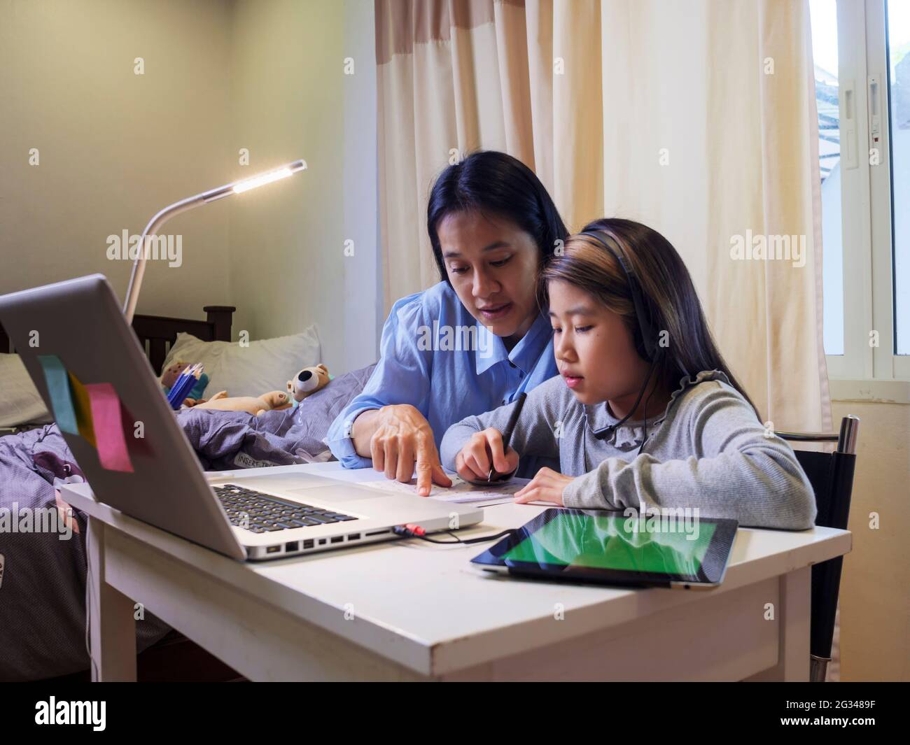 Asian young little girl using pencil to do homework with her mother ...