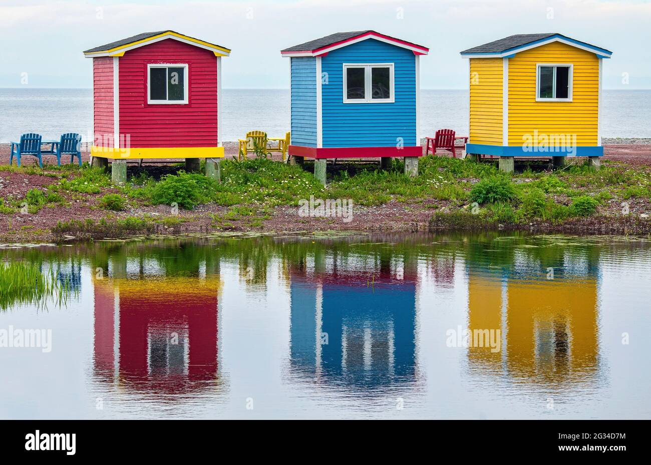 Three colorful small huts on a Newfoundland beach cast reflections on ...