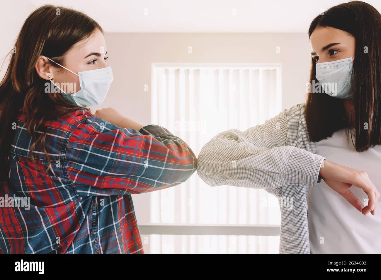 Two smiling girls in protective face mask say hello in safe way with ...